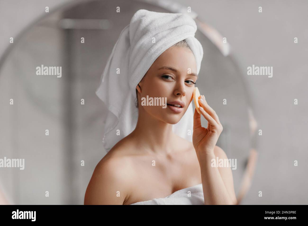 Pretty lady using cosmetic sponge enjoying facial skincare routine ...