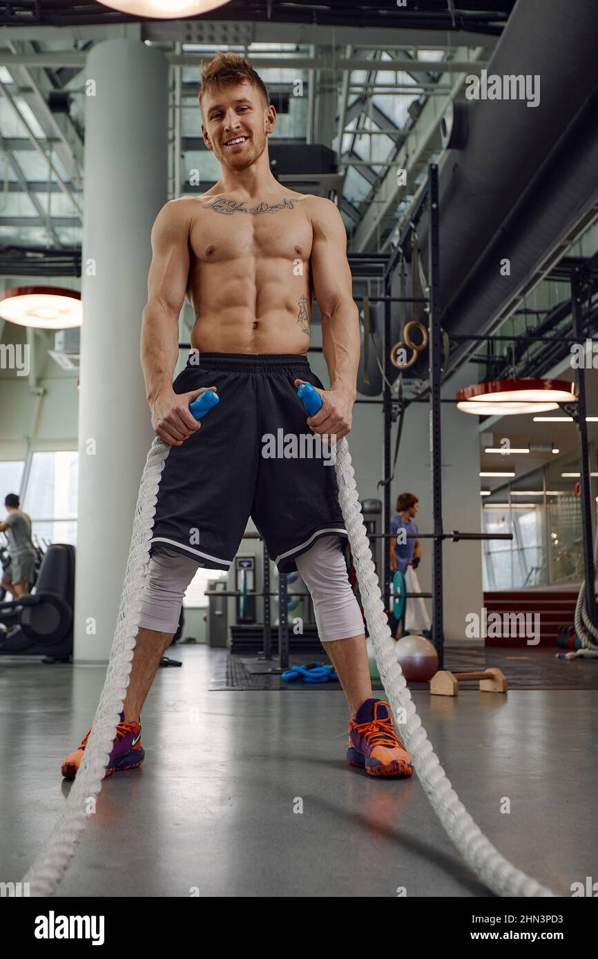Muscular powerful aggressive man training with rope in functional ...