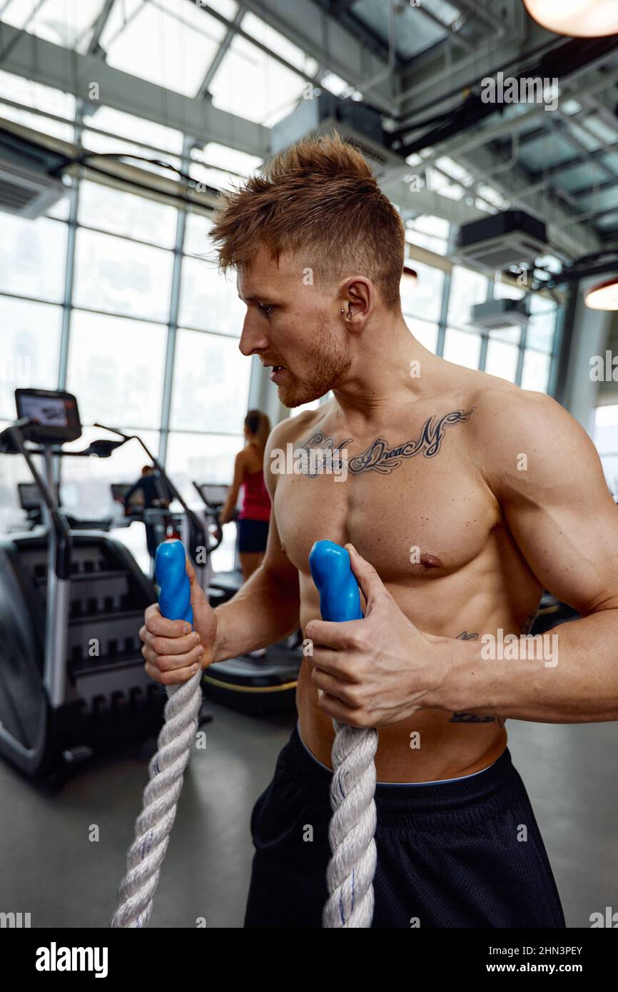 Muscular powerful aggressive man training with rope in functional ...