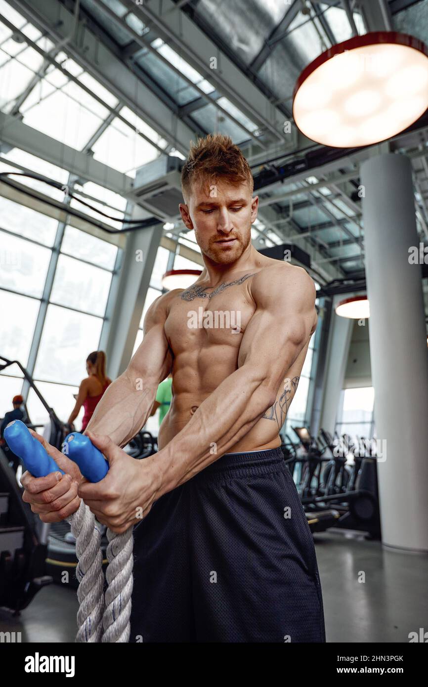 Muscular powerful aggressive man training with rope in functional ...