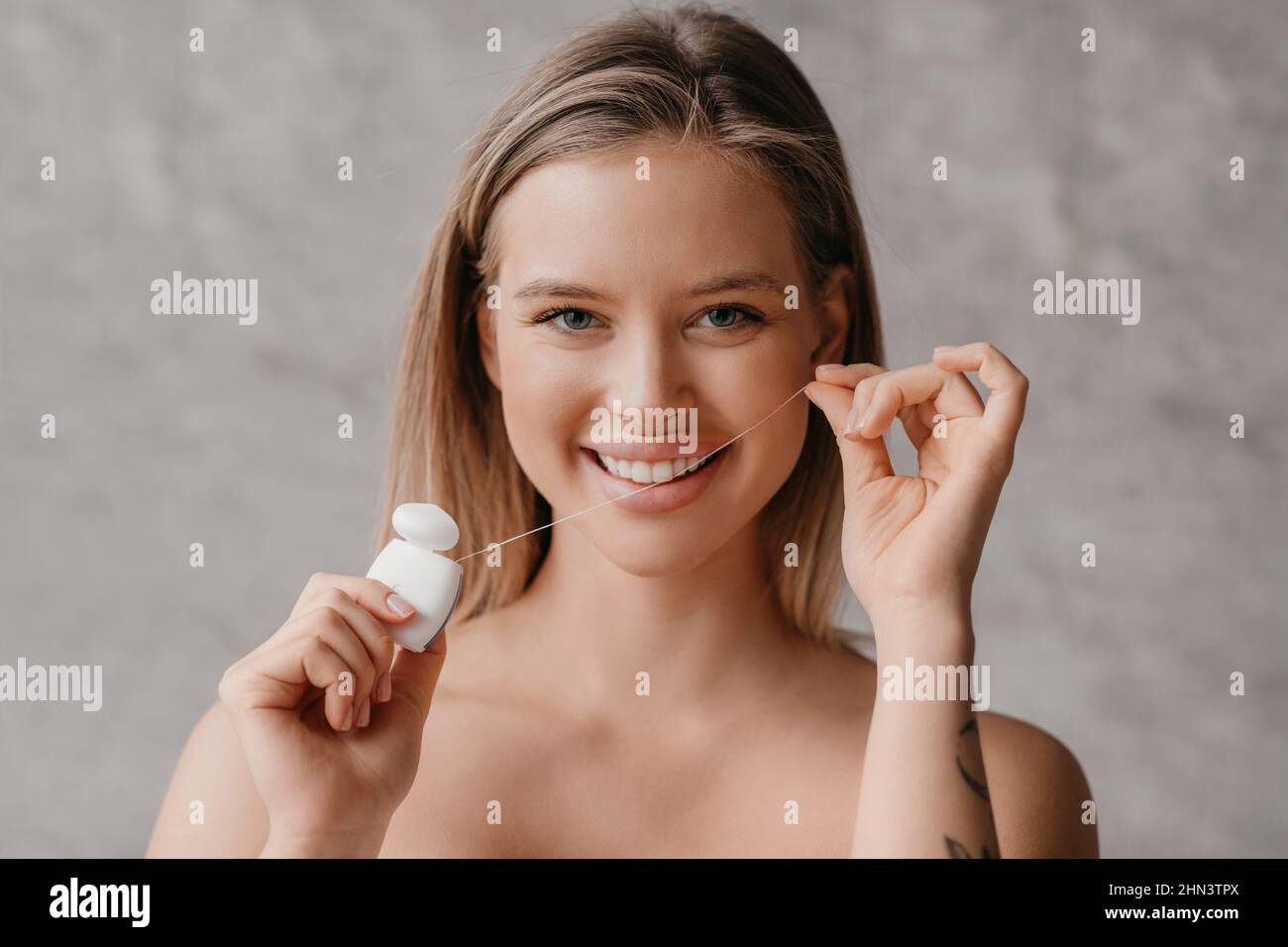 Portrait of smiling lady using dental floss at home, looking at camera ...