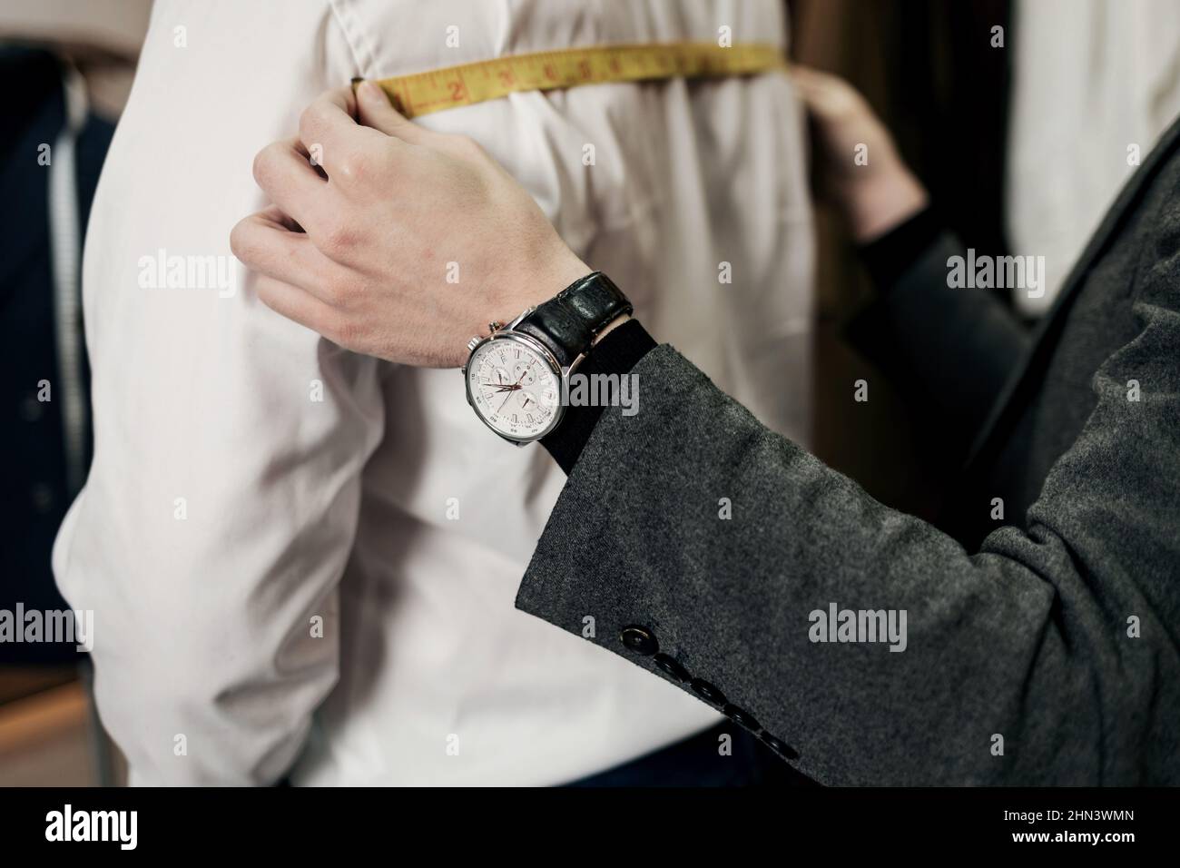 Young fashionable designer measuring clients back while standing in his ...