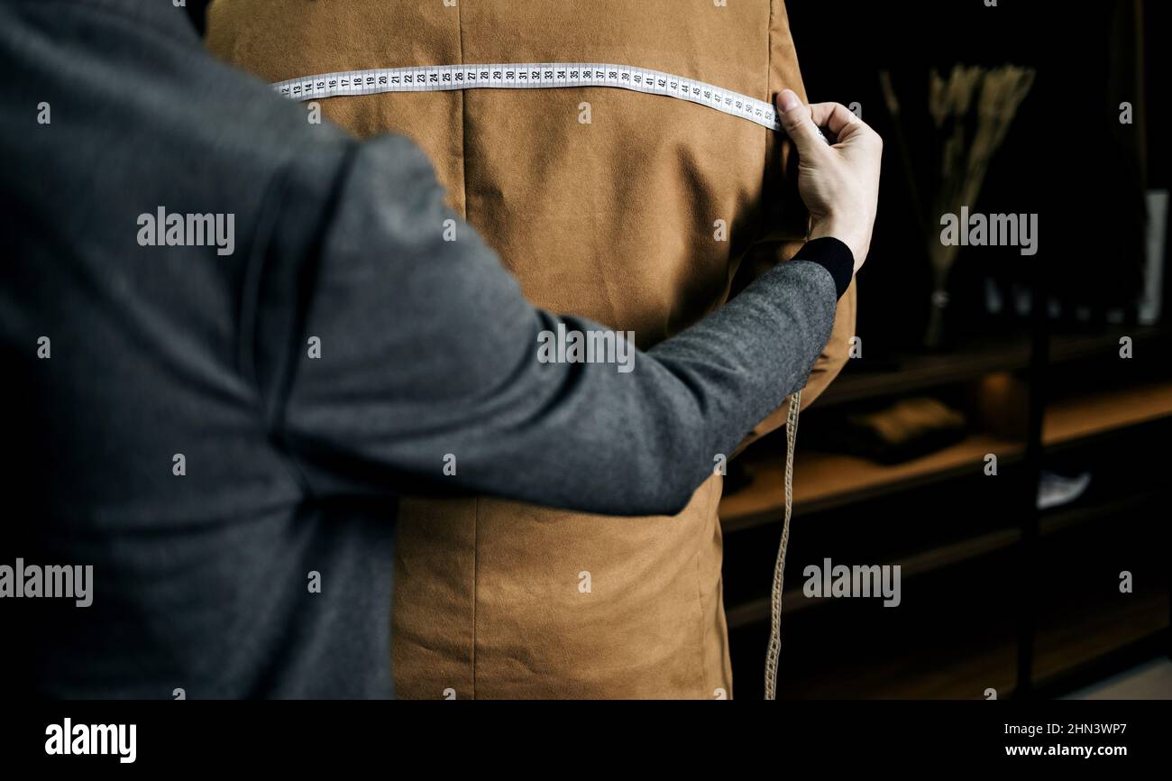portrait of tailor fitting bespoke suit to model. back view ...
