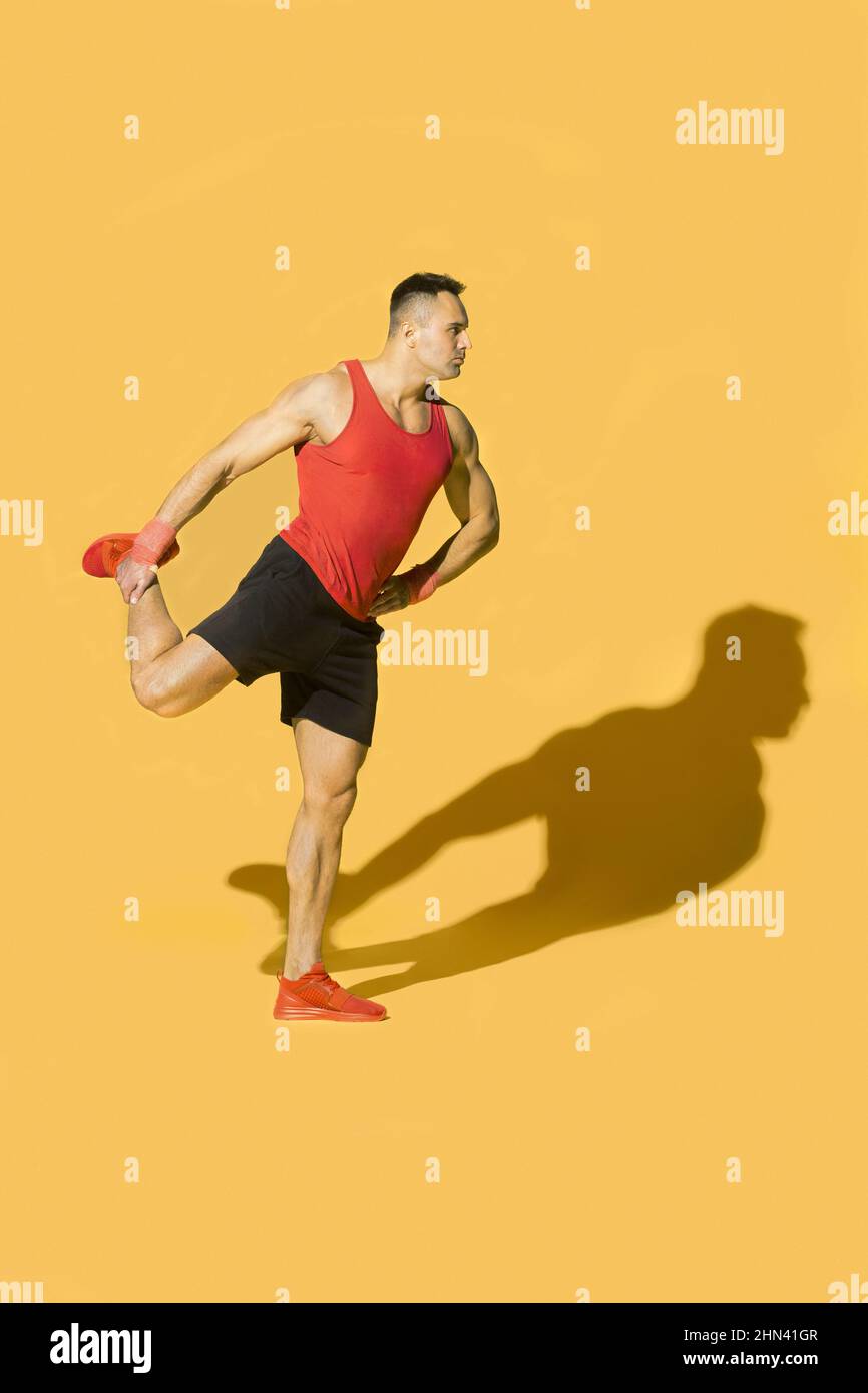 Strong, athletic man with shadow stretching leg against yellow ...
