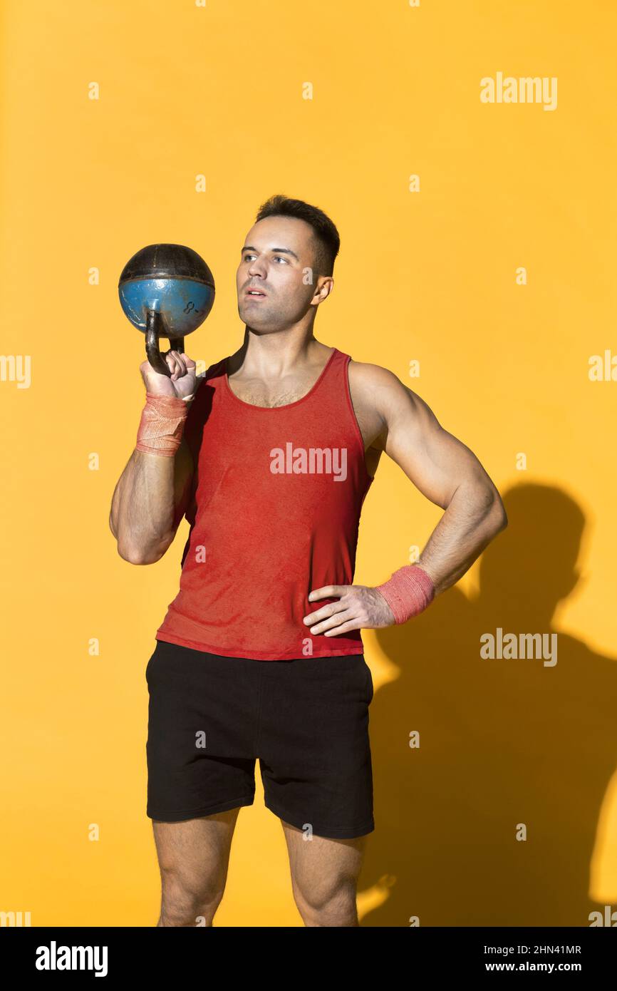 Strong, athletic man lifting kettle bell against yellow background ...