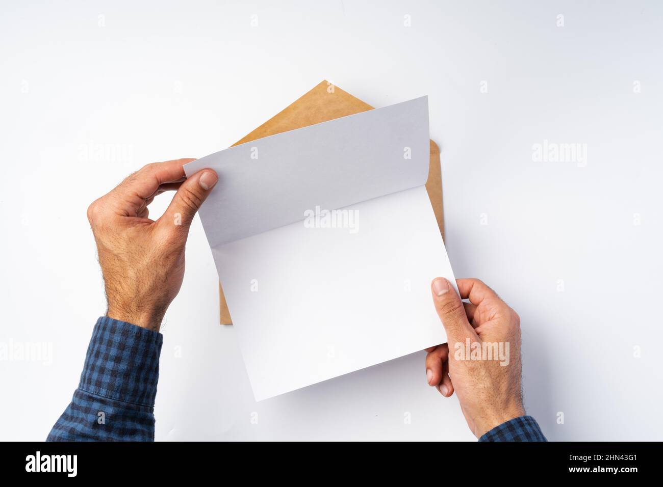Top view of male hands hold (open) an envelope above white background ...
