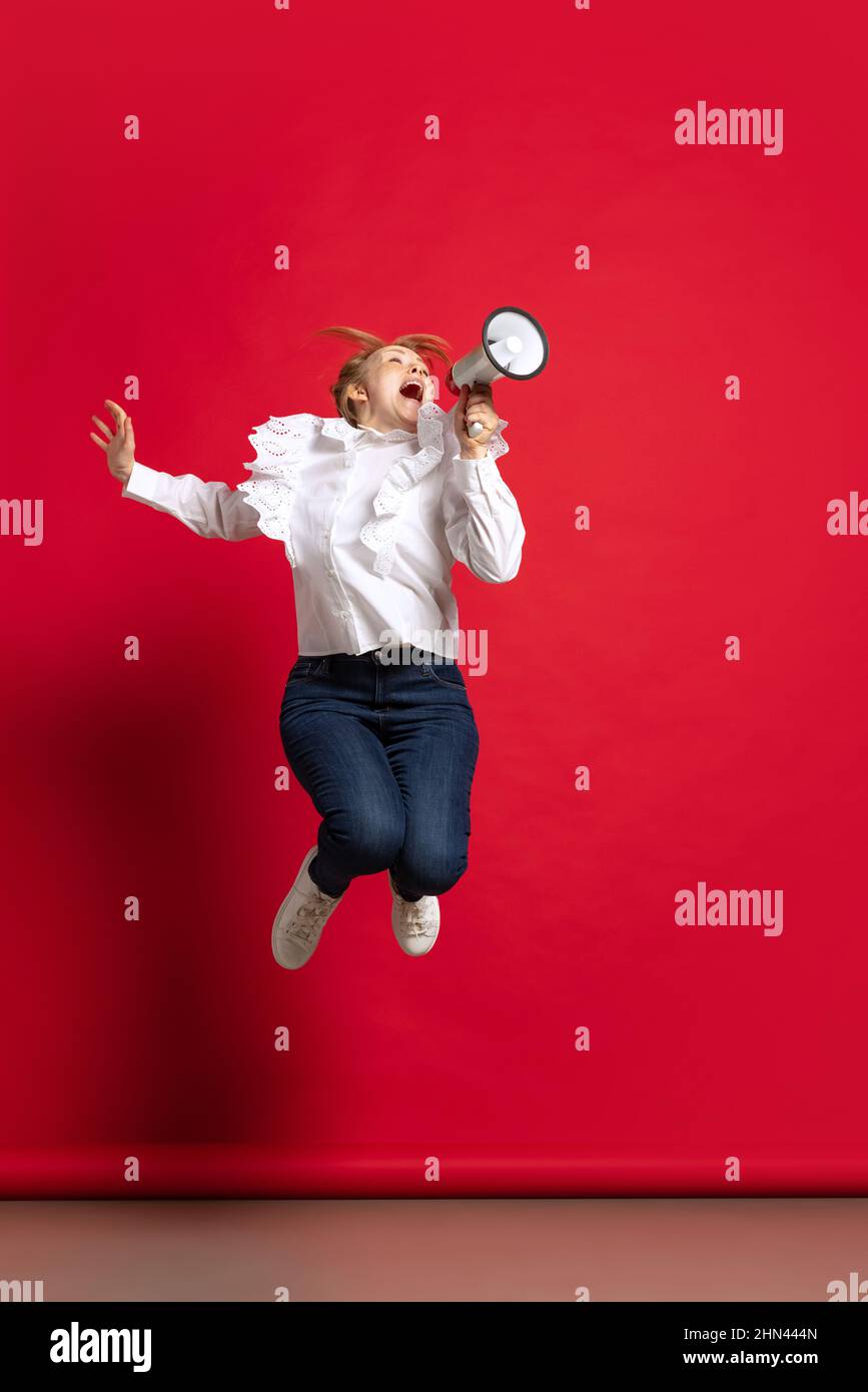 Full-length portrait of excited young girl jumping isolated on red ...