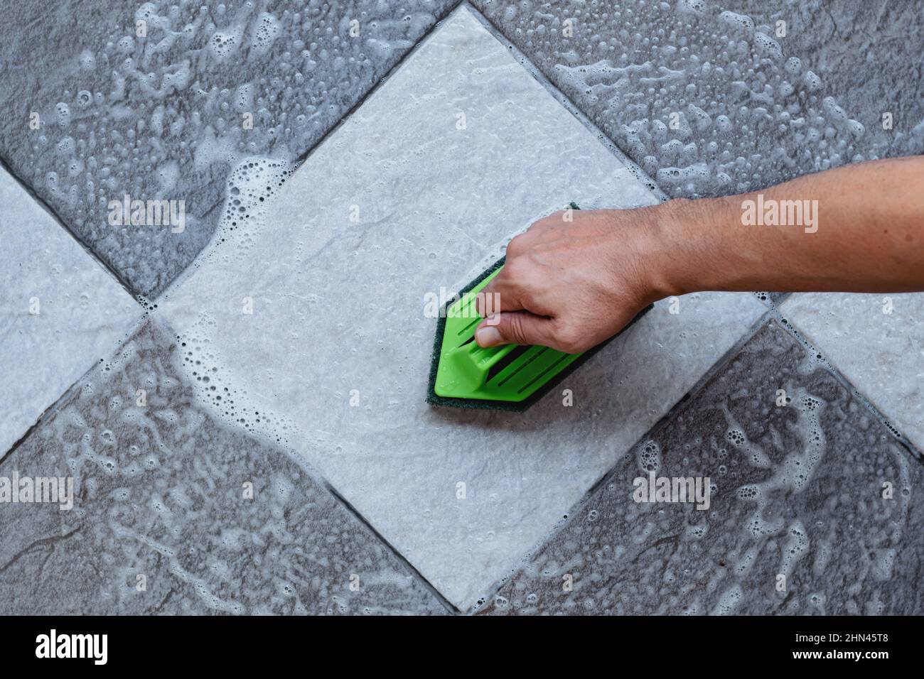 Top view of a human hand are using a green color plastic floor scrubber ...
