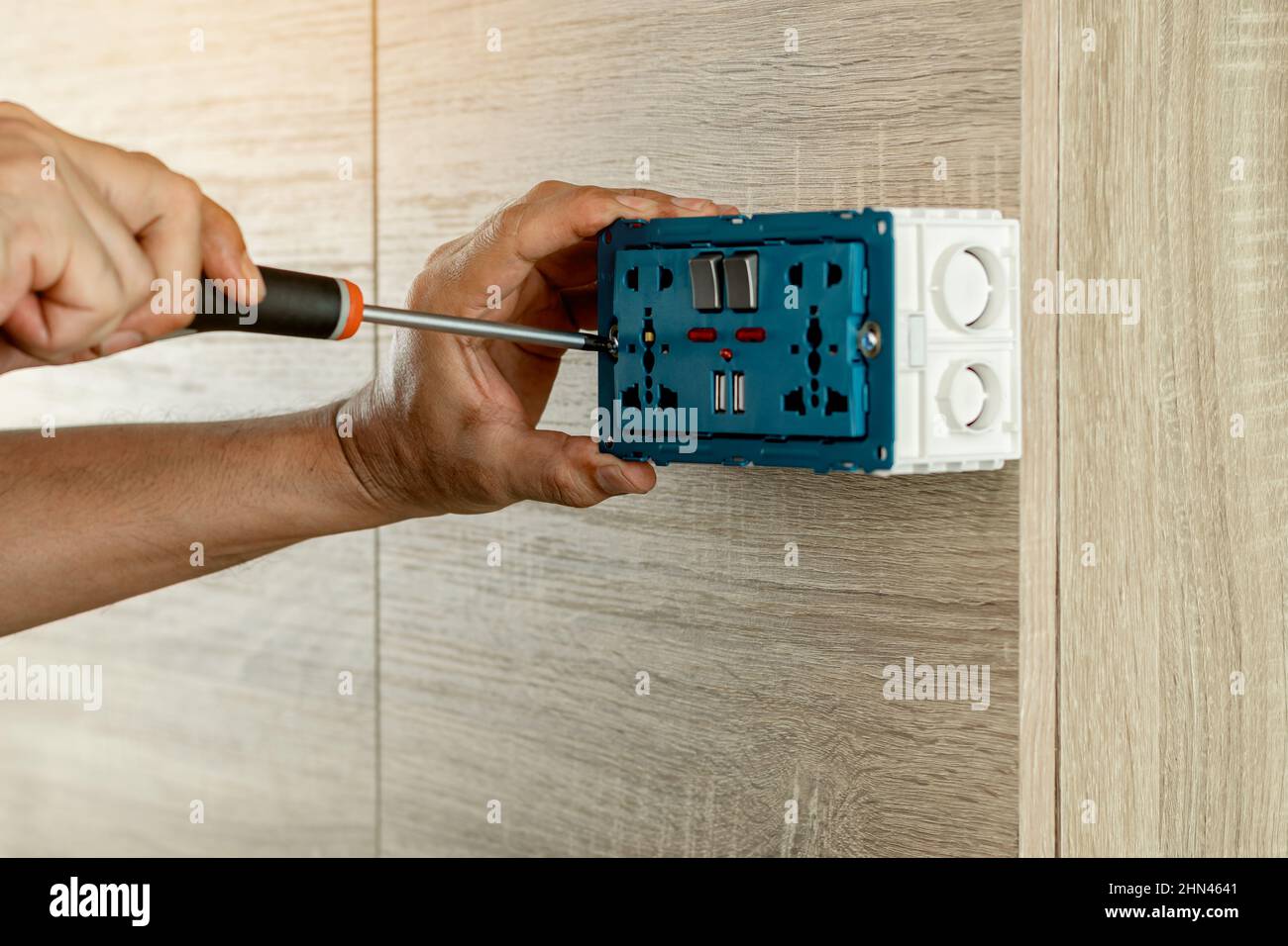 Electrician is using a screwdriver to install the electric power socket ...