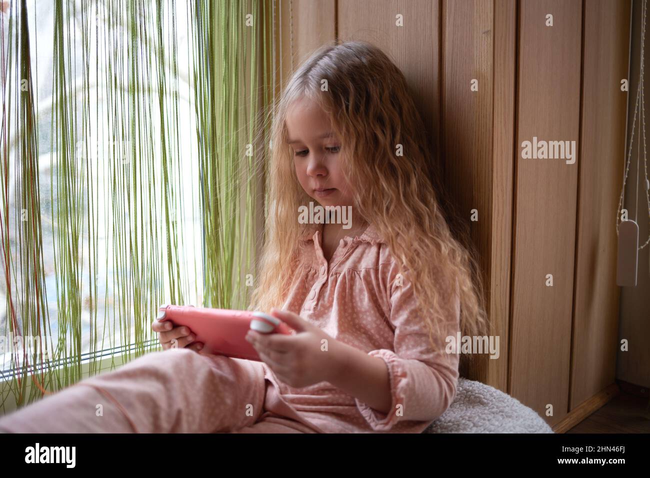little cute girl plays a game console sitting on the windowsill Stock ...