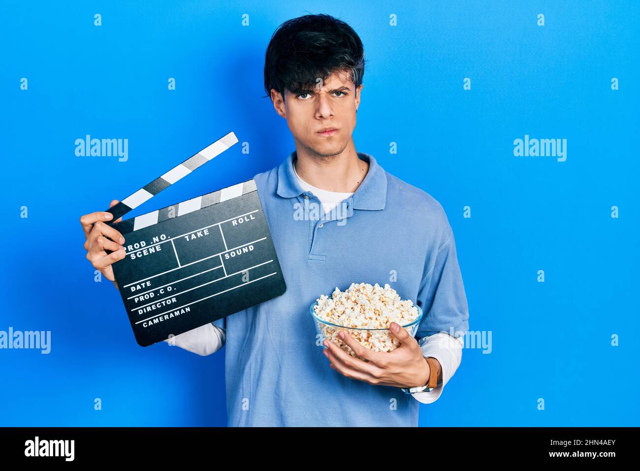 Handsome hipster young man eating popcorn holding cinema clapboard ...