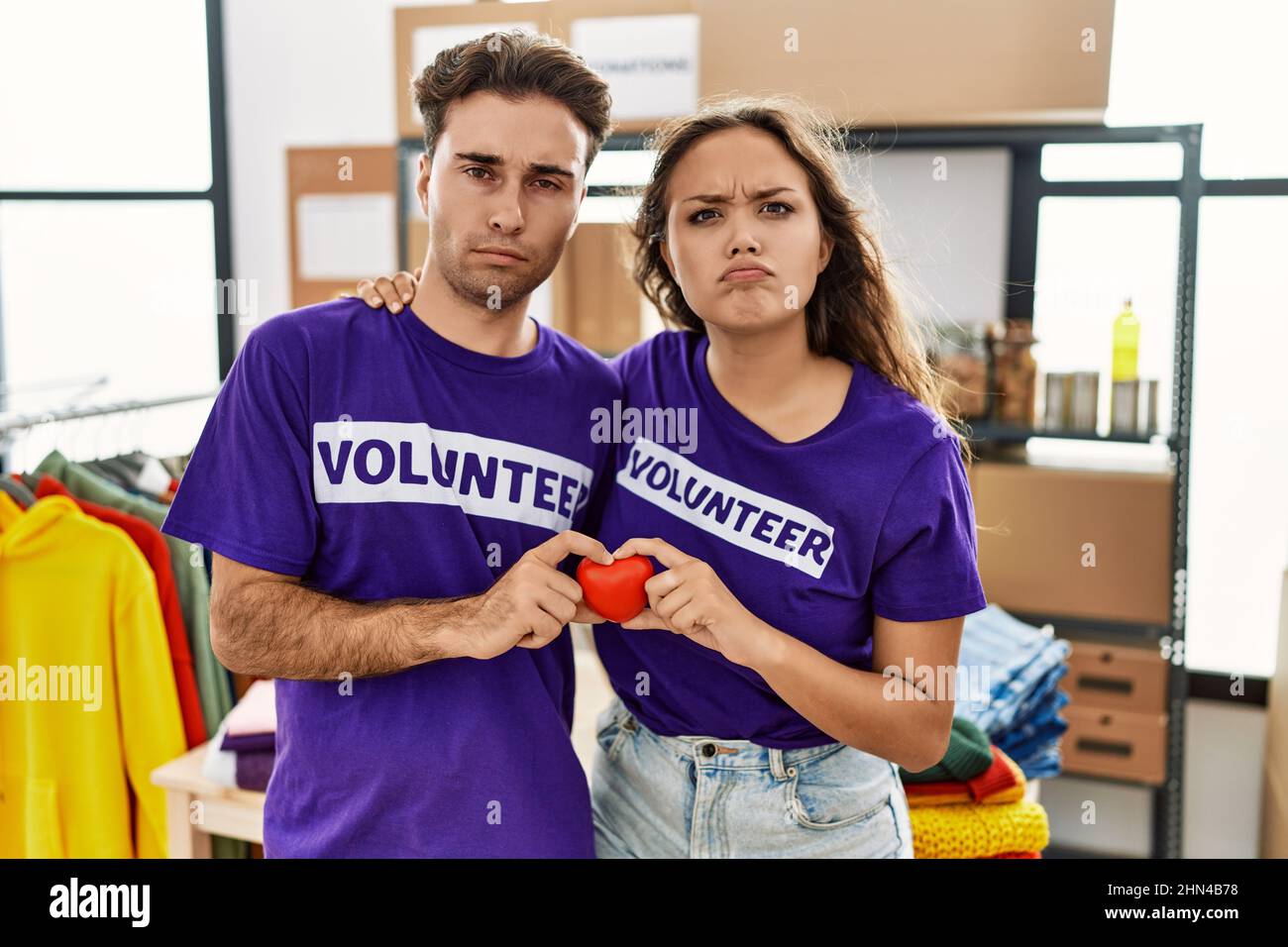 Young hispanic couple wearing volunteer t shirt holding heart skeptic ...