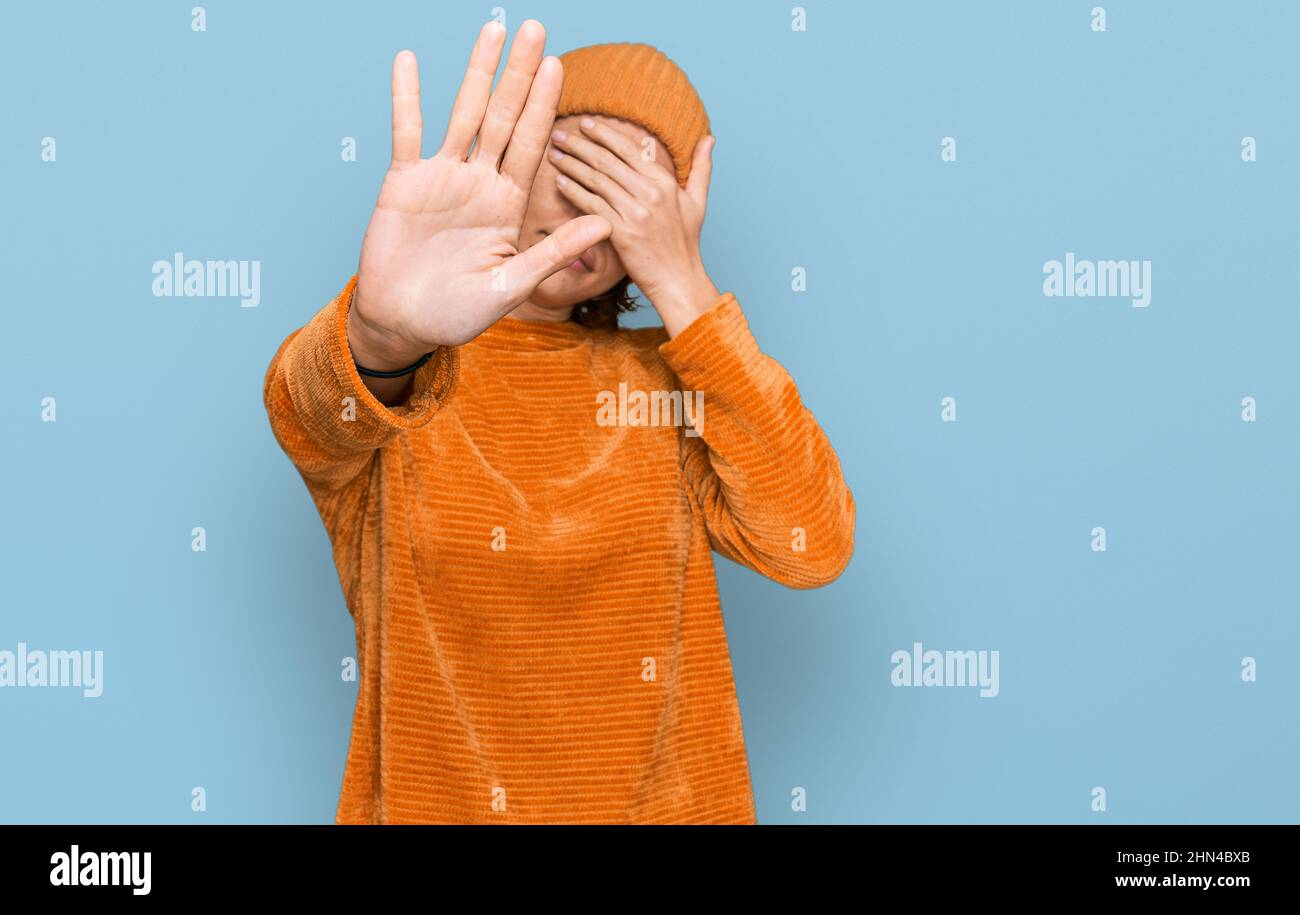 Young hispanic woman wearing casual clothes and wool cap covering eyes ...