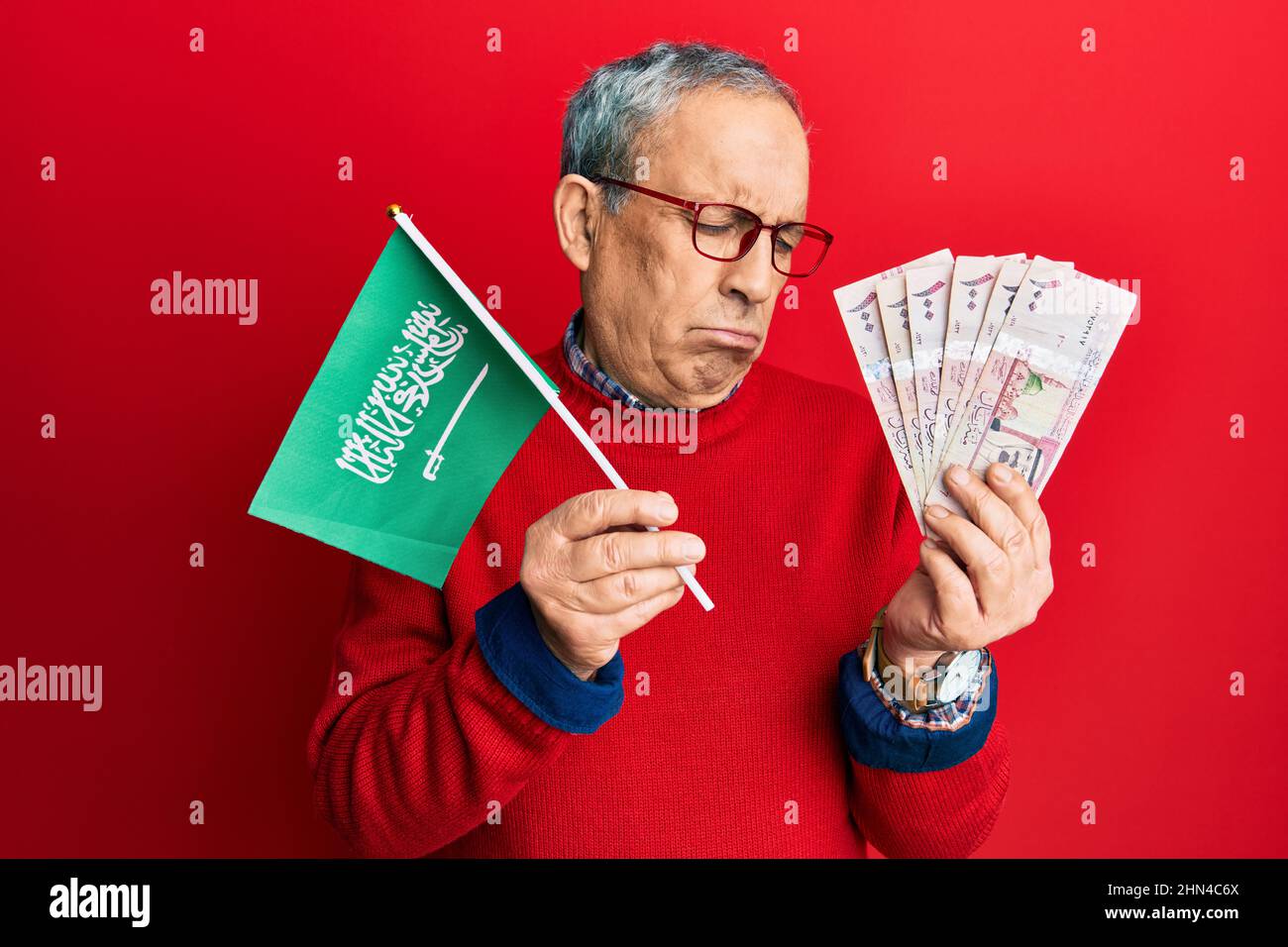 Handsome senior man with grey hair holding saudi arabia flag and riyal ...