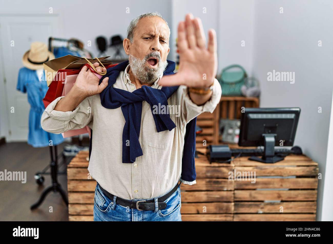 Handsome senior man holding shopping bags at boutique shop doing stop ...