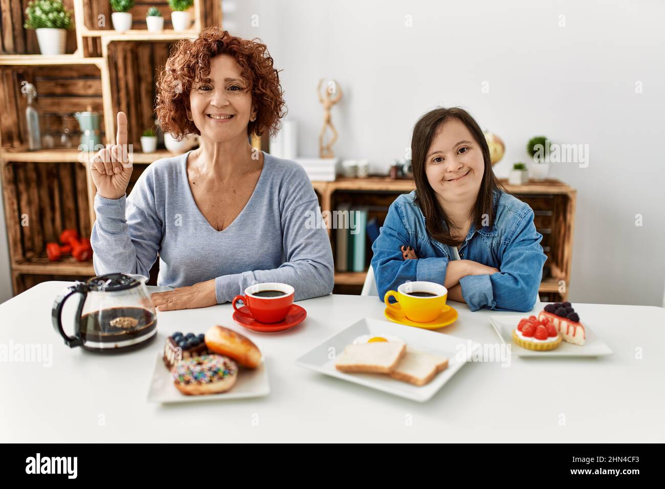 Family of mother and down syndrome daughter sitting at home eating ...