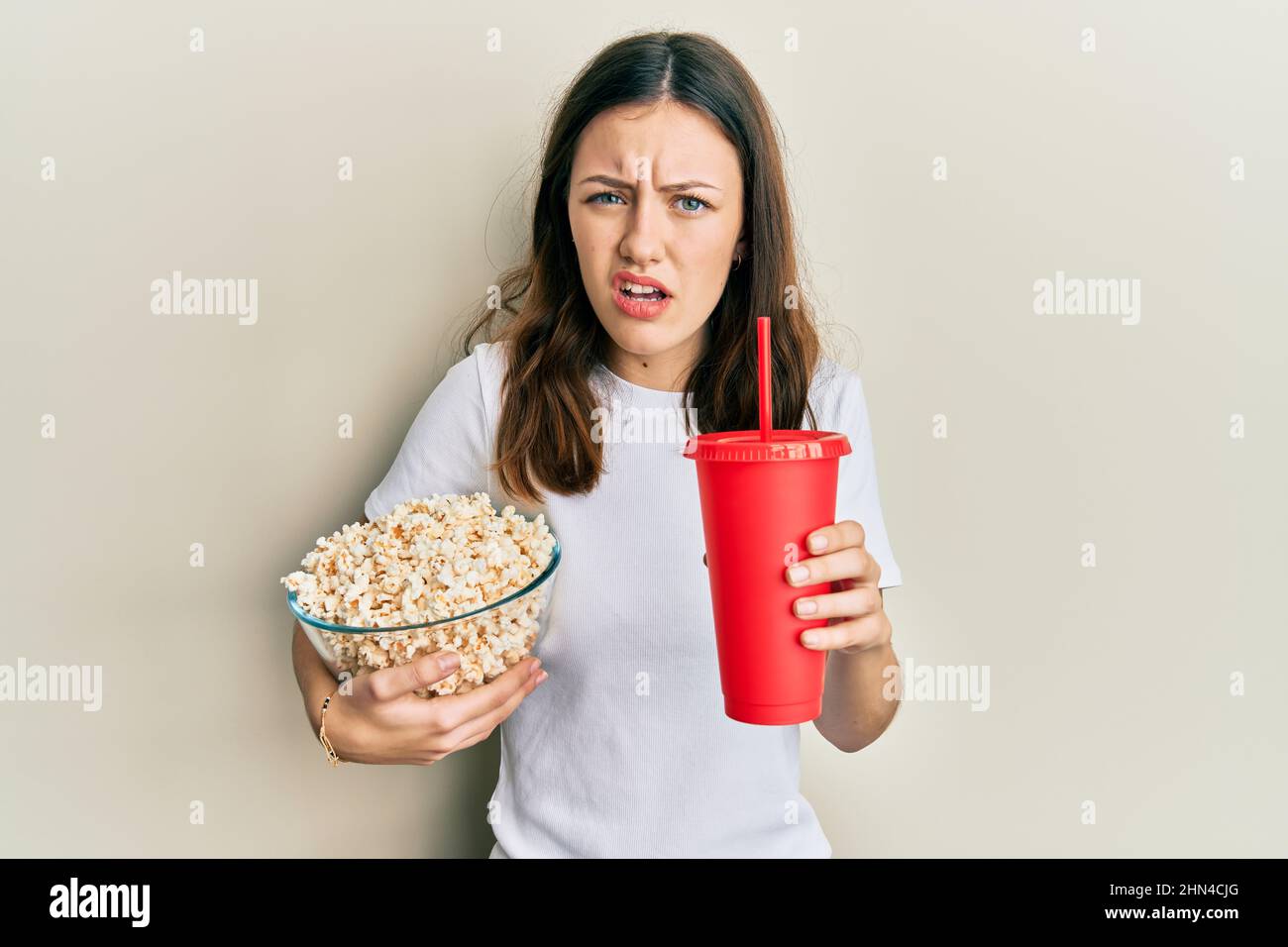 Young brunette woman eating popcorn and drinking soda clueless and ...