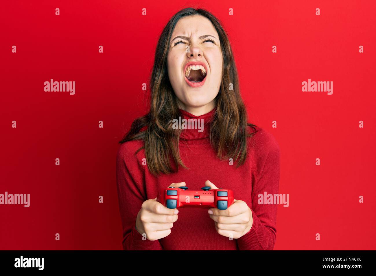 Young brunette woman playing video game holding controller angry and ...