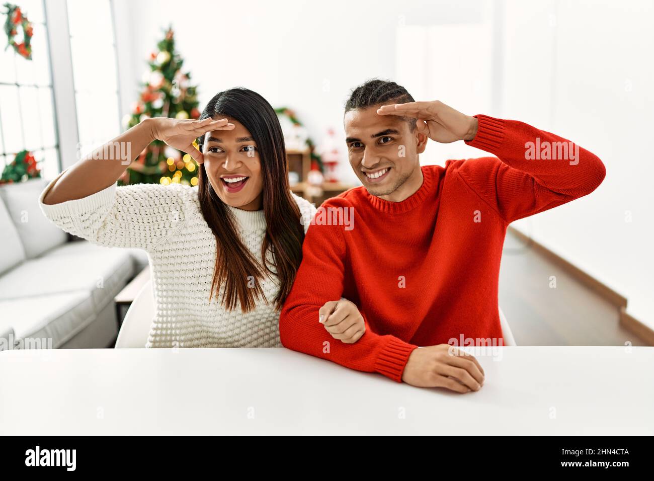 Young latin couple sitting on the table by christmas tree very happy ...