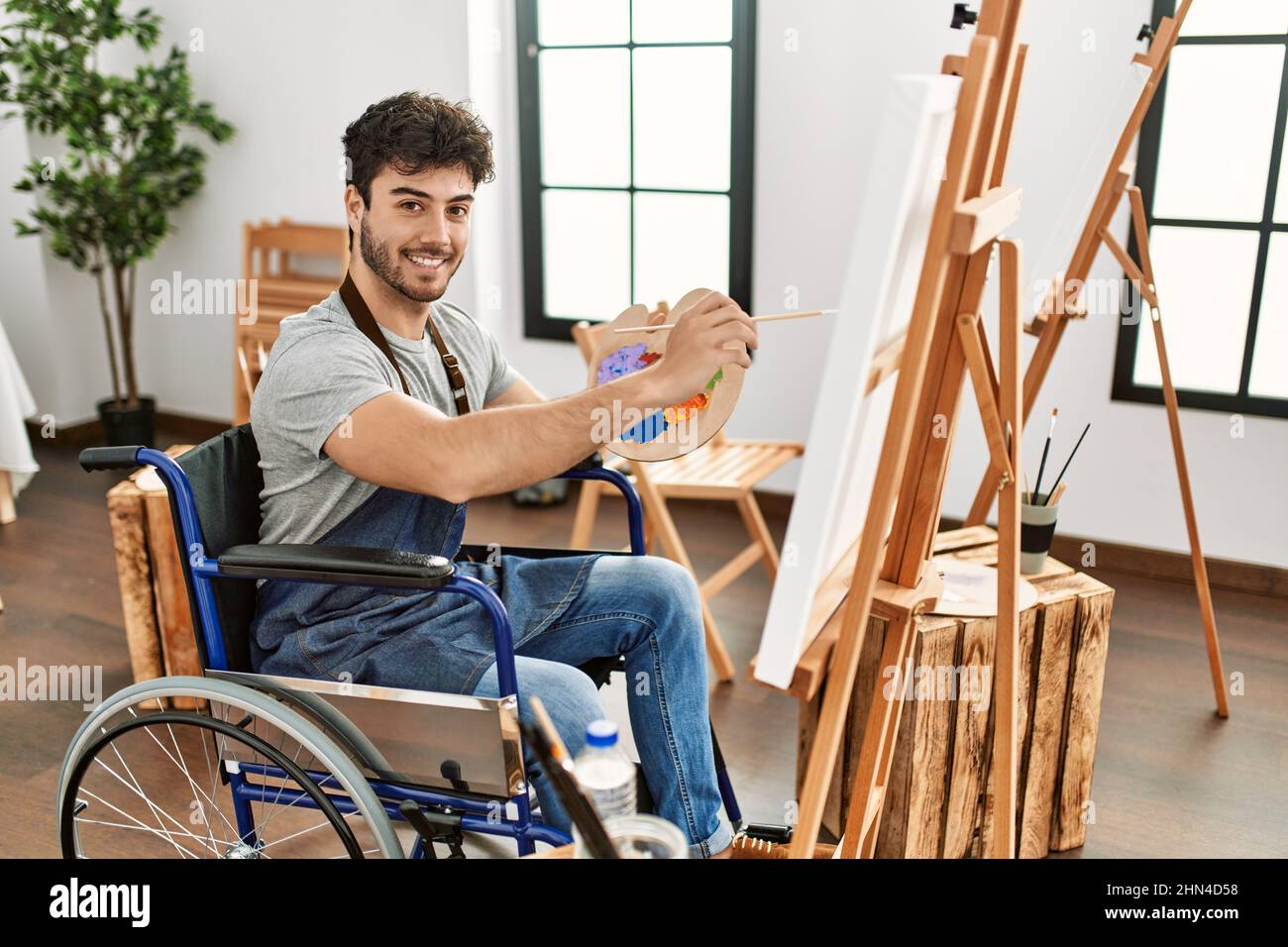 Young hispanic artist disabled man smiling happy painting at art studio ...