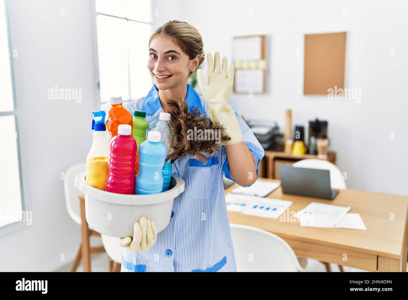 Young blonde woman wearing cleaner uniform holding cleaning products ...