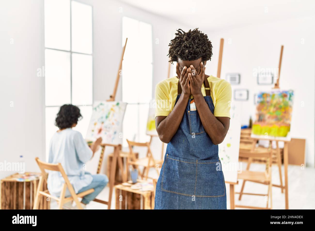 African young man standing at art studio with sad expression covering ...
