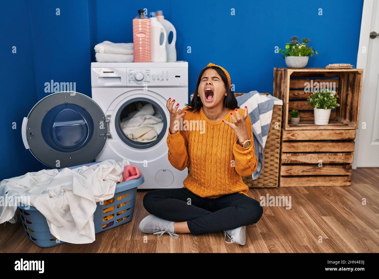Young hispanic woman doing laundry crazy and mad shouting and yelling ...