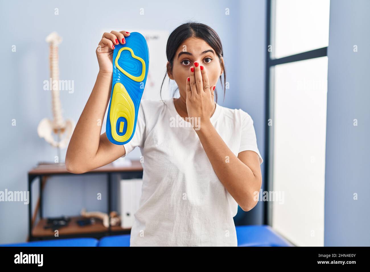 Young hispanic woman holding shoe insole at physiotherapy clinic ...