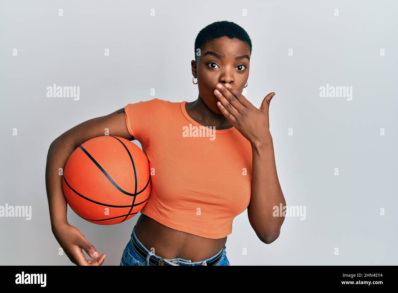Young african american woman holding basketball ball covering mouth ...