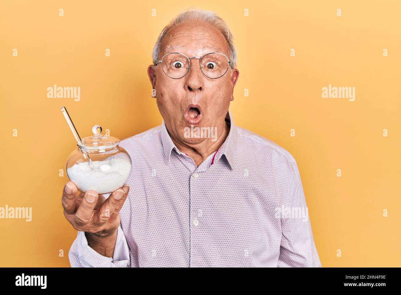 Senior man with grey hair holding bowl with sugar scared and amazed ...