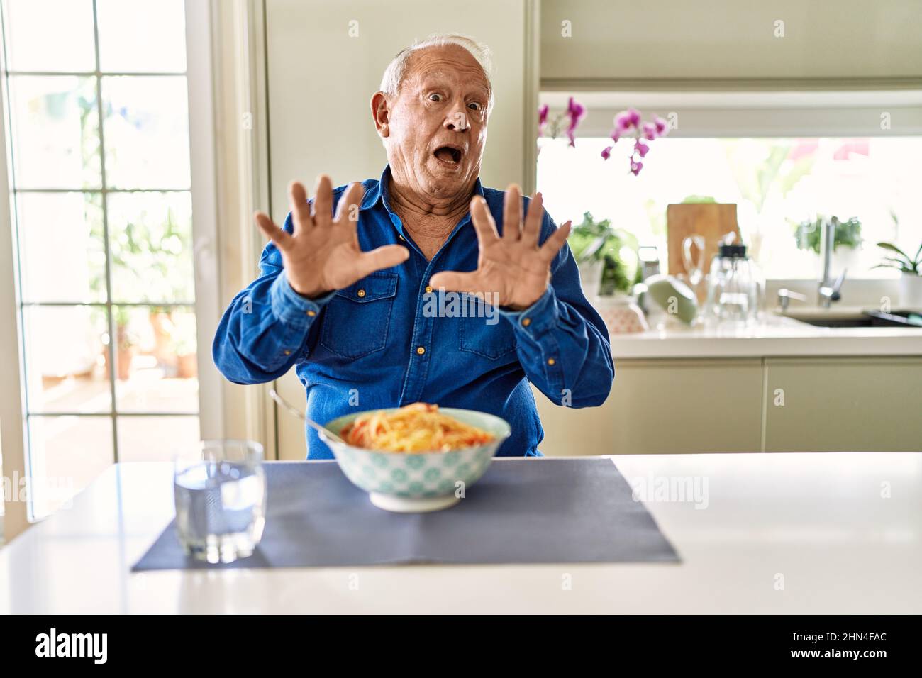 Senior man with grey hair eating pasta spaghetti at home afraid and ...