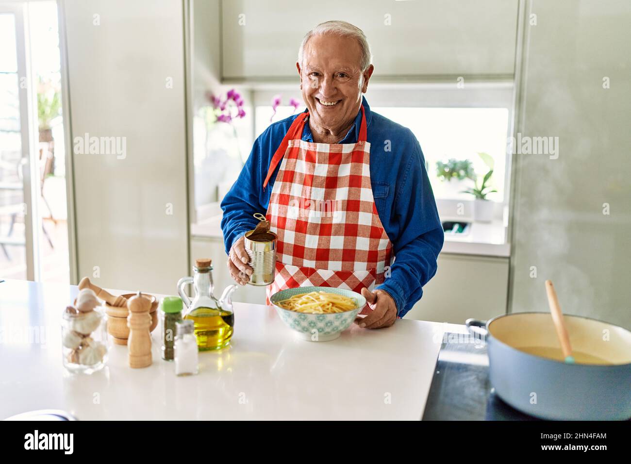 Senior man smiling confident pouring tomato sauce on spaghetti at ...