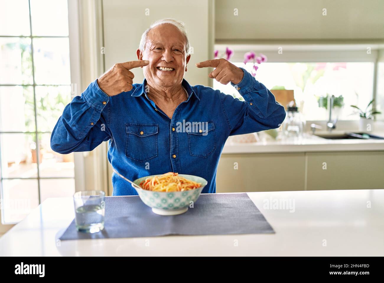 Senior man with grey hair eating pasta spaghetti at home smiling ...