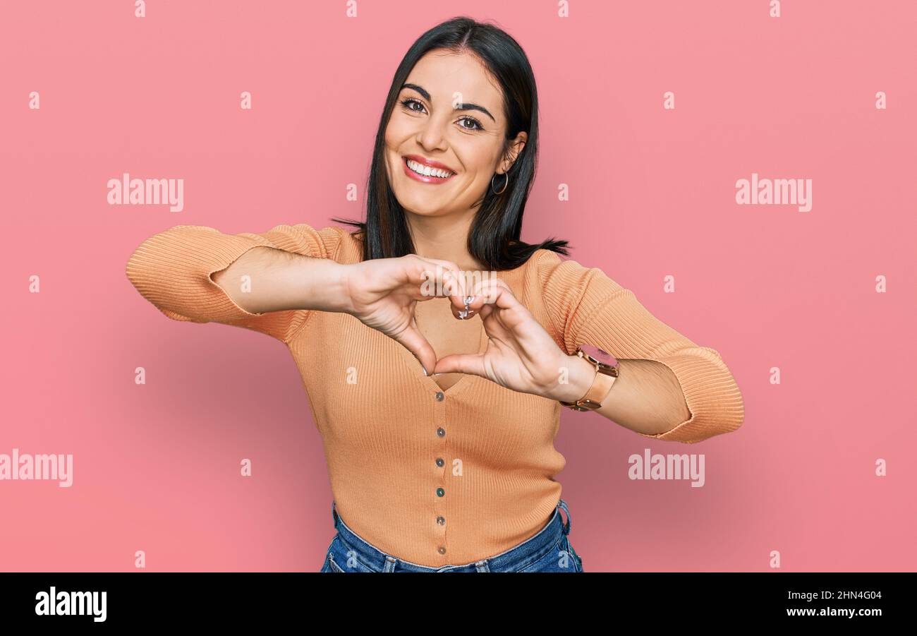 Young hispanic woman wearing casual clothes smiling in love doing heart ...