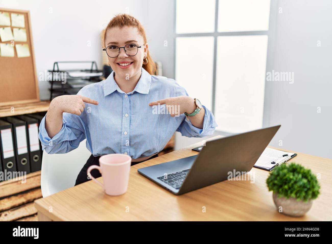 Young redhead woman working at the office using computer laptop looking ...