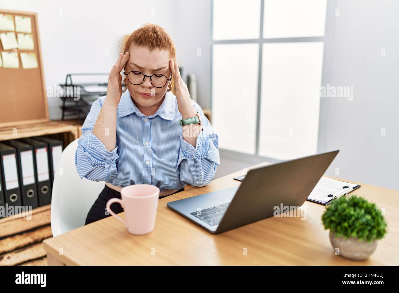 Young redhead woman working at the office using computer laptop with ...