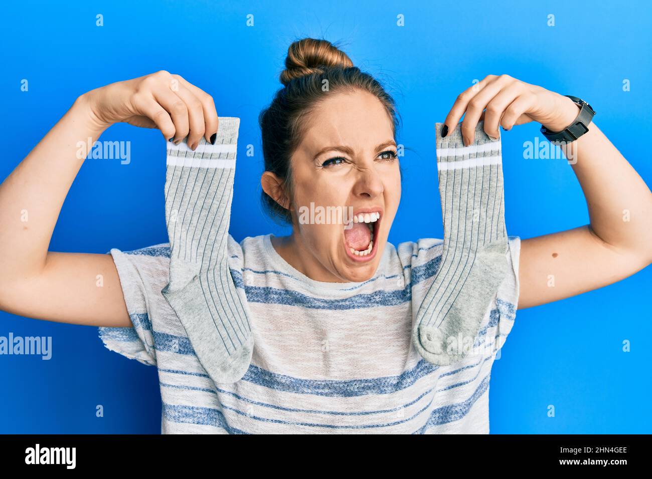 Young blonde woman holding socks angry and mad screaming frustrated and ...
