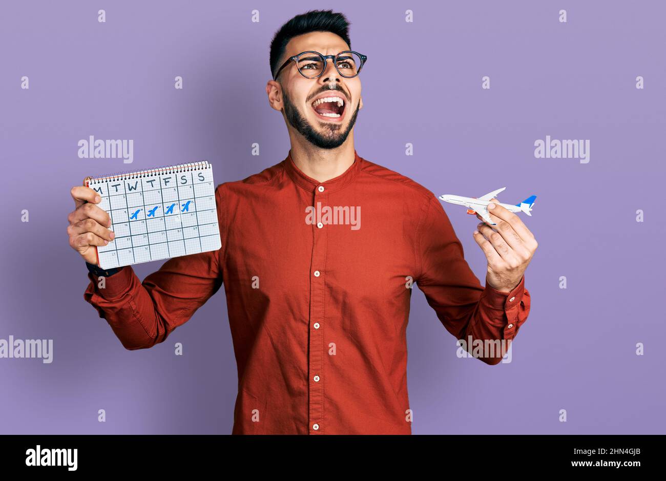 Young hispanic man with beard holding plane toy and travel calendar ...