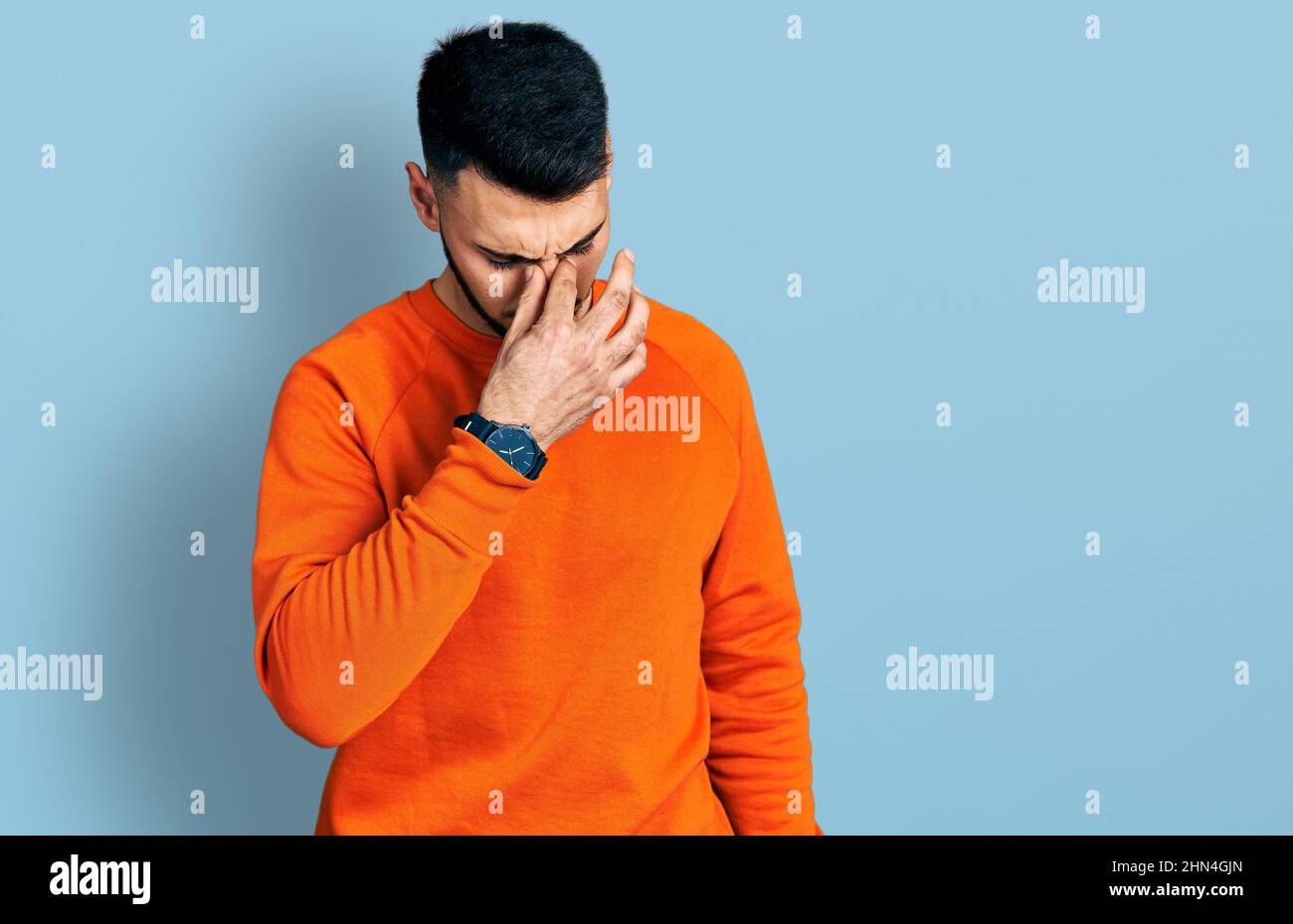 Young hispanic man with beard wearing casual orange sweater tired ...