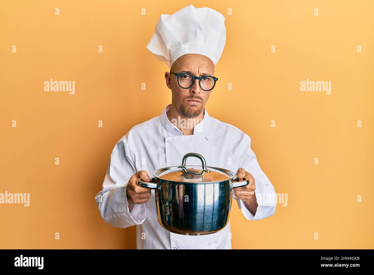 Bald man with beard wearing professional cook holding cooking pot ...
