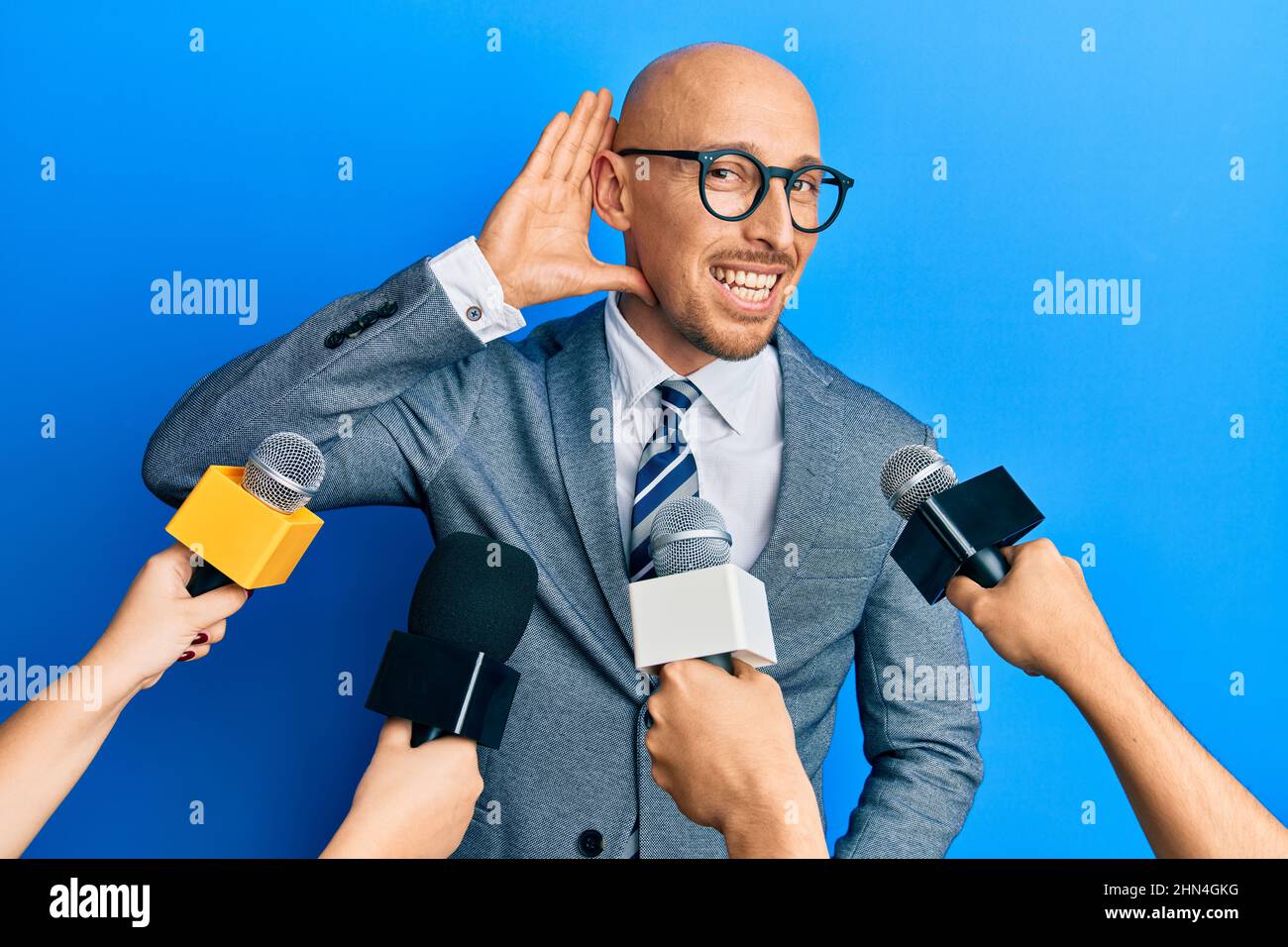Bald man with beard being interviewed by reporters holding microphones ...