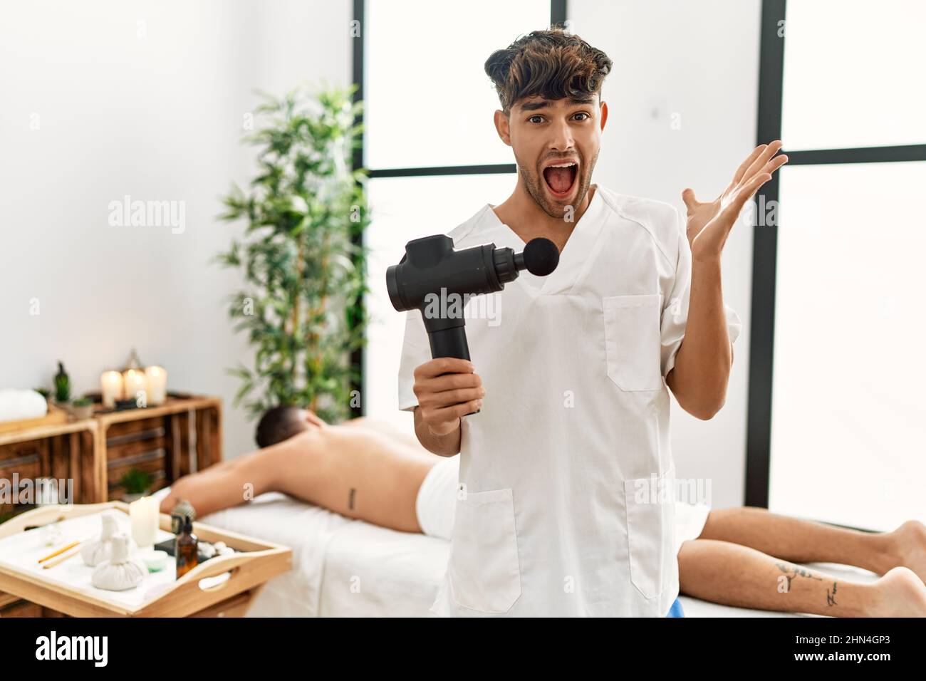 Young hispanic man holding therapy massage gun at wellness center ...