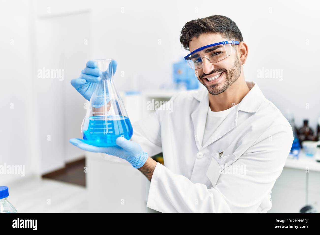 Handsome hispanic man working as scientific holding erlenmeyer flask at ...