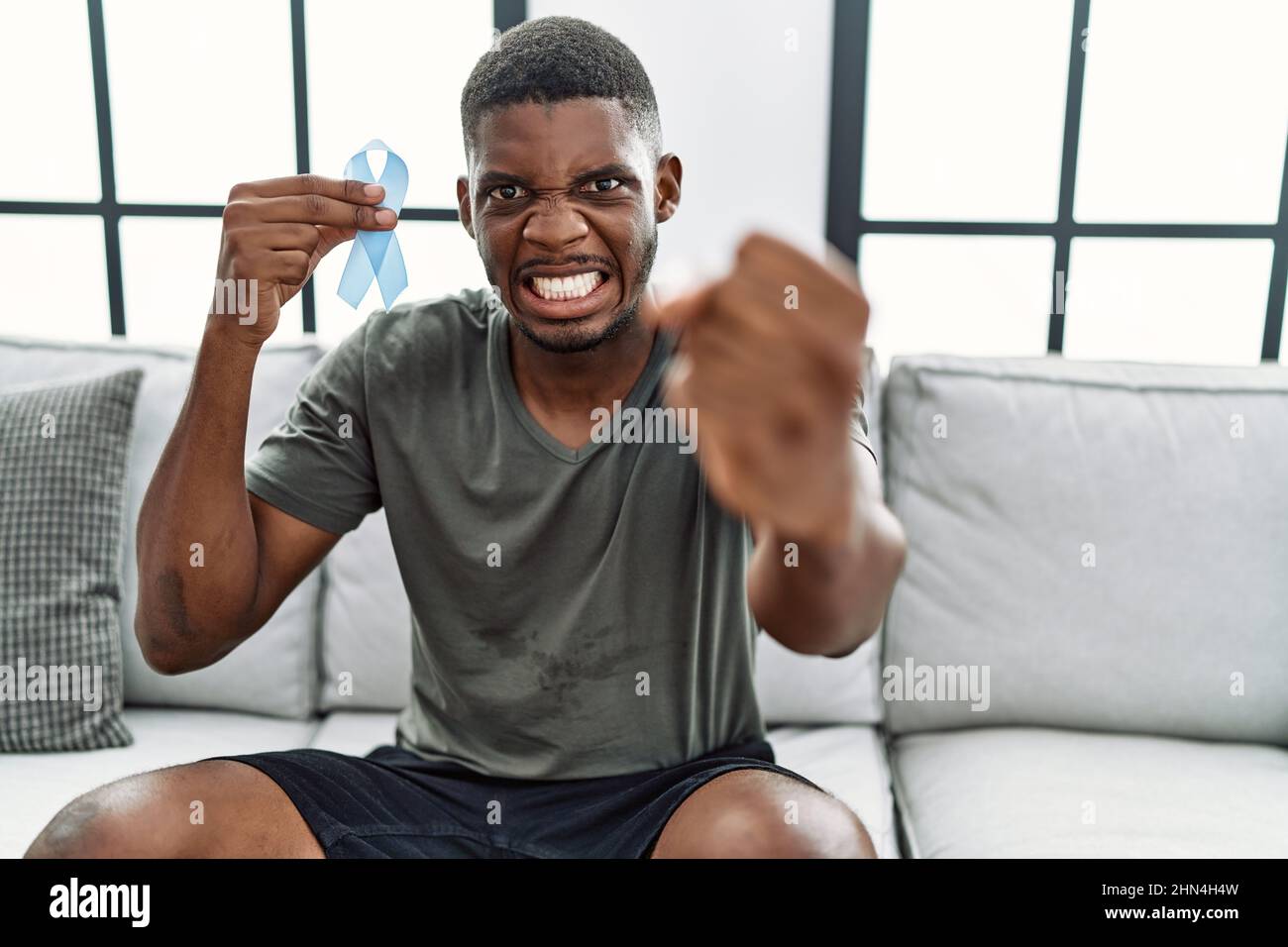 Young african american man holding blue ribbon sitting on the sofa at ...