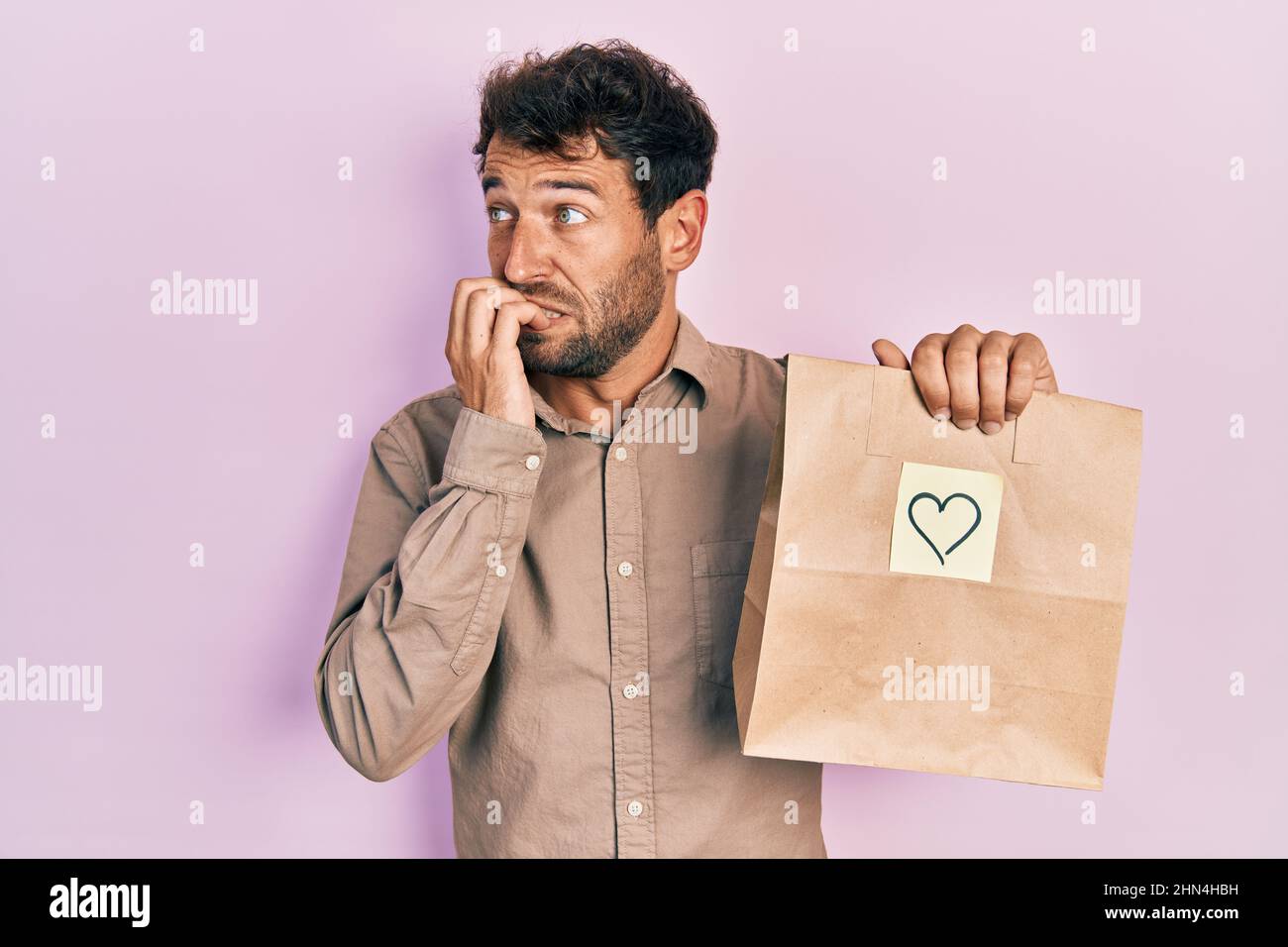 Handsome man with beard holding delivery paper bag with heart reminder ...