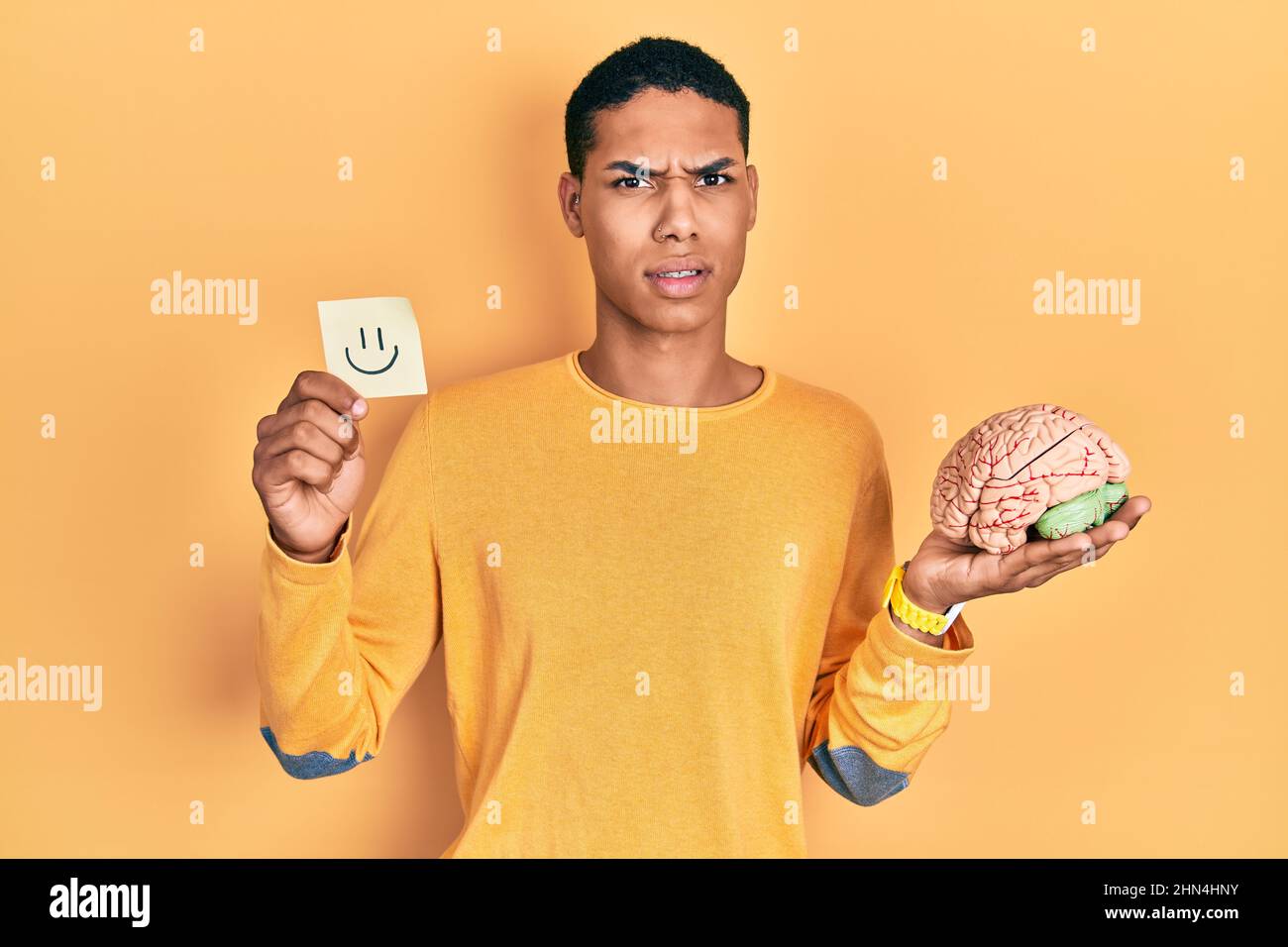 Young african american guy holding smile reminder and brain clueless ...