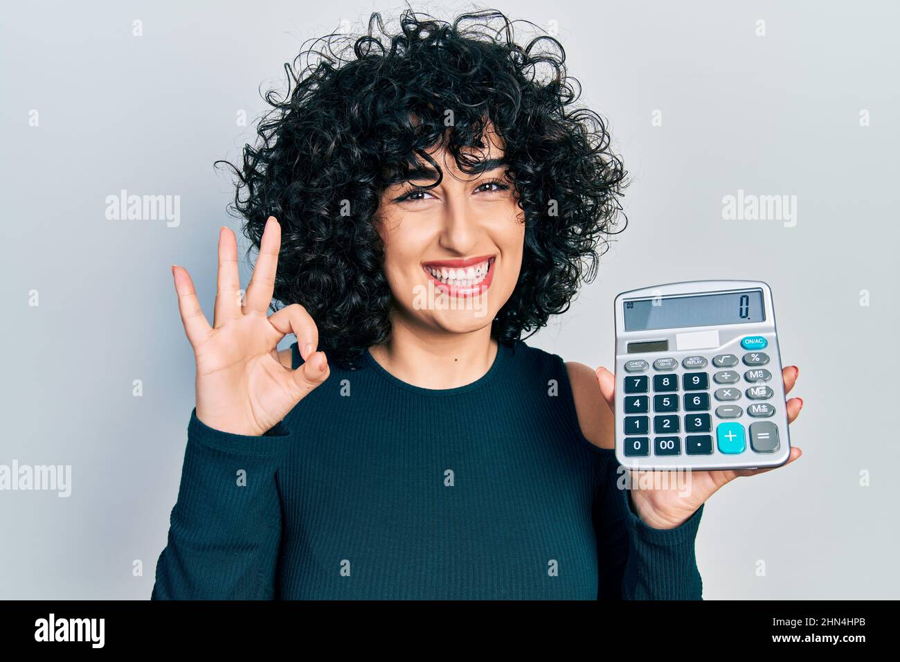 Young middle east woman showing calculator device doing ok sign with ...