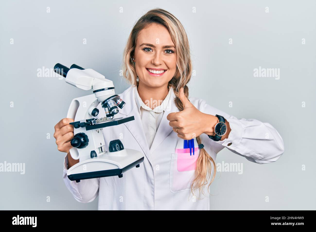 Beautiful young blonde woman holding microscope smiling happy and ...