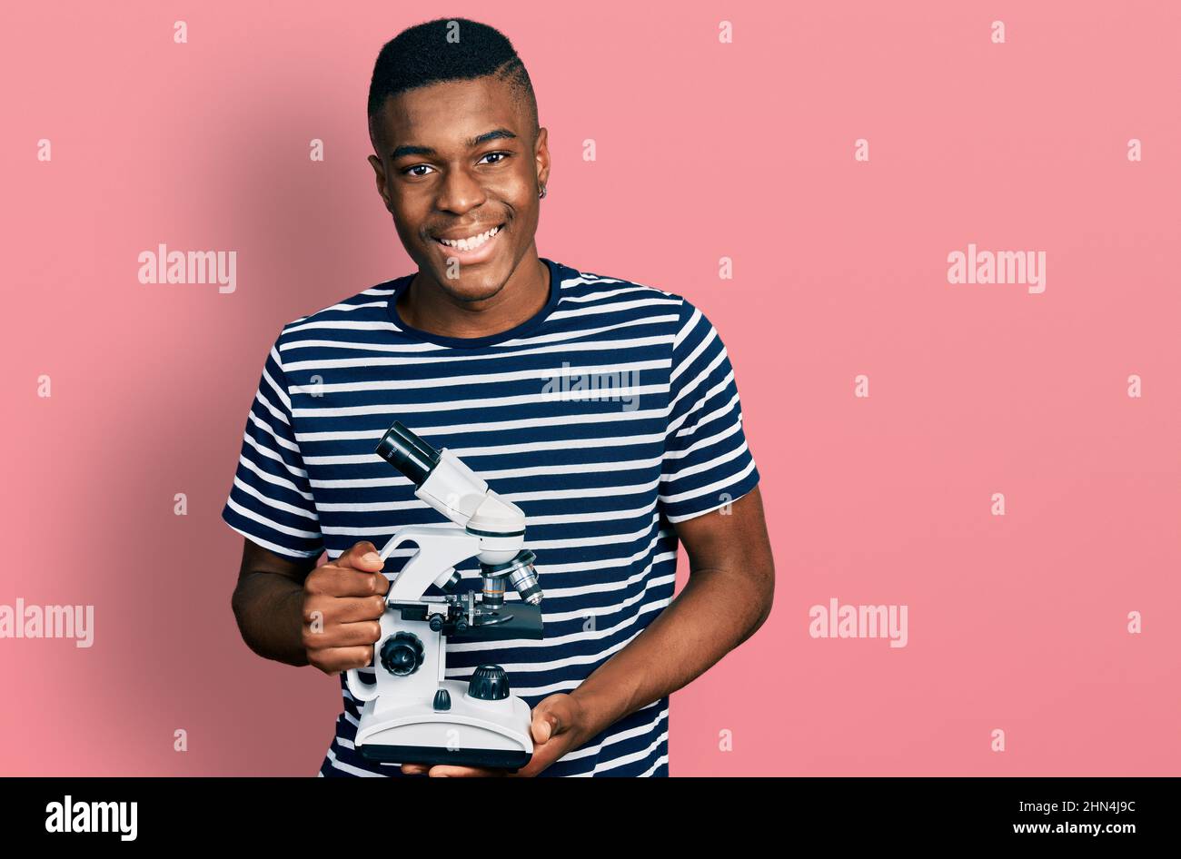 Young african american man holding microscope looking positive and ...