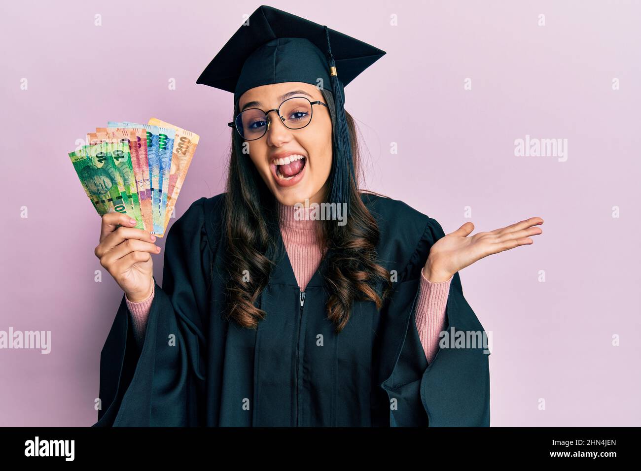 Young hispanic woman wearing graduation uniform holding south africa ...
